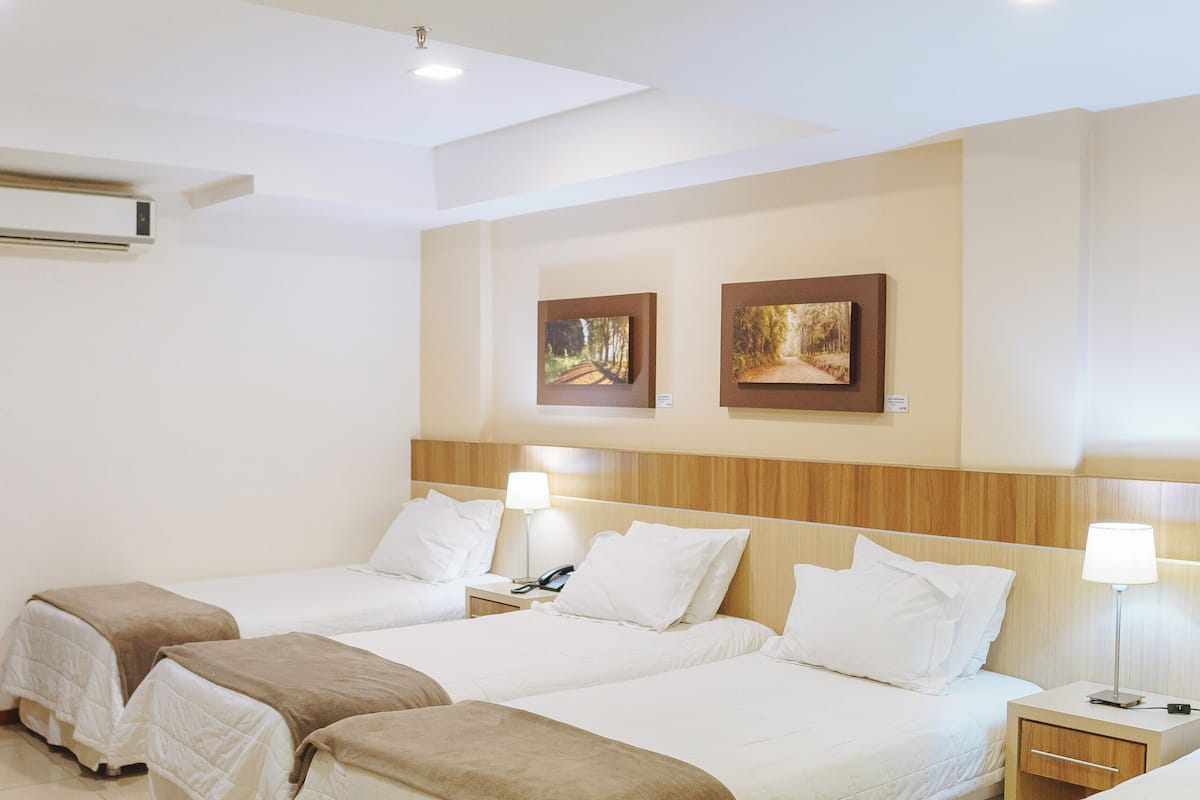 Quarto de hotel com quatro camas, cabeceira de madeira, obra de arte na parede e mesa de cabeceira com abajur.