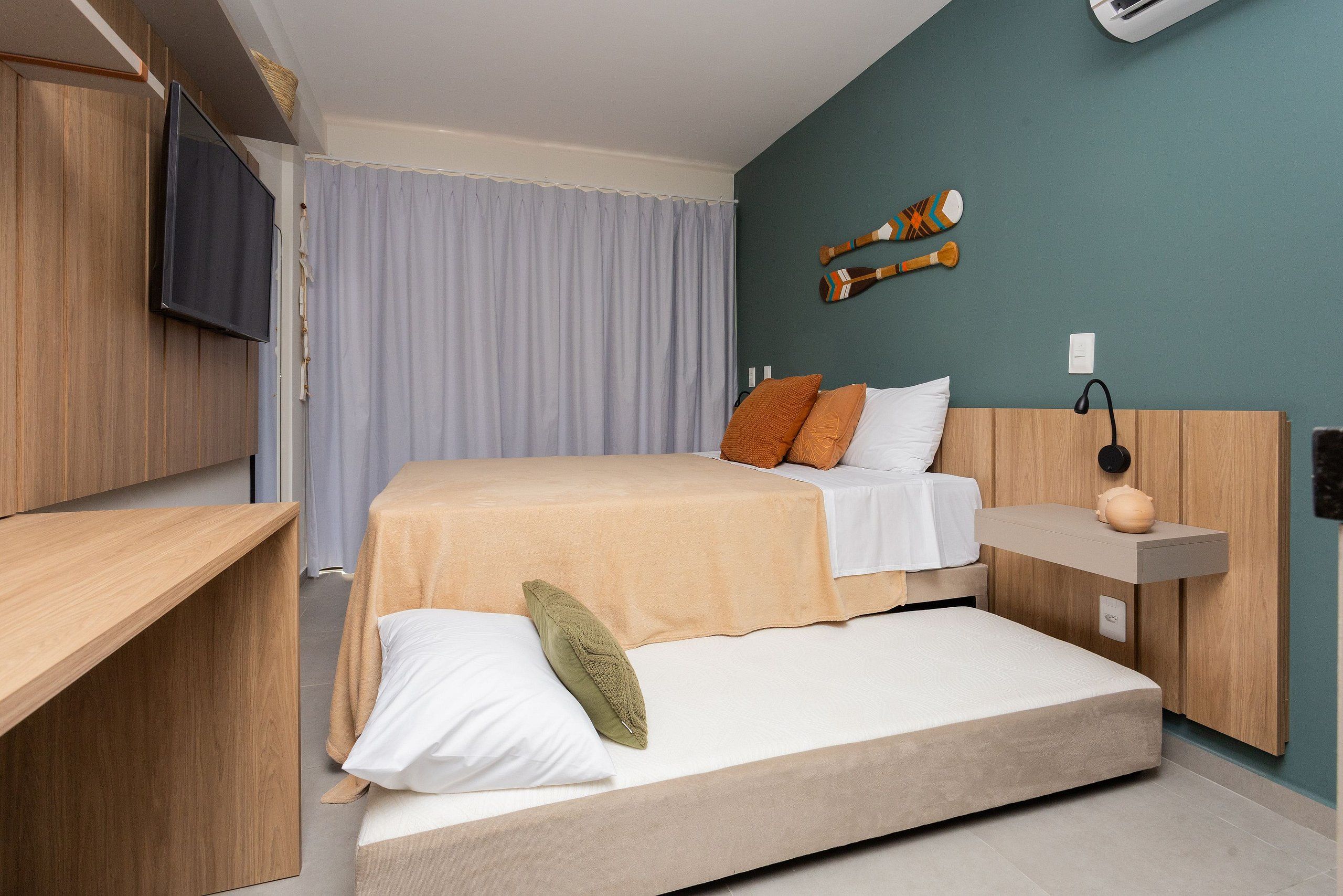 Quarto moderno com cama, mesa de cabeceira e televisão na parede.