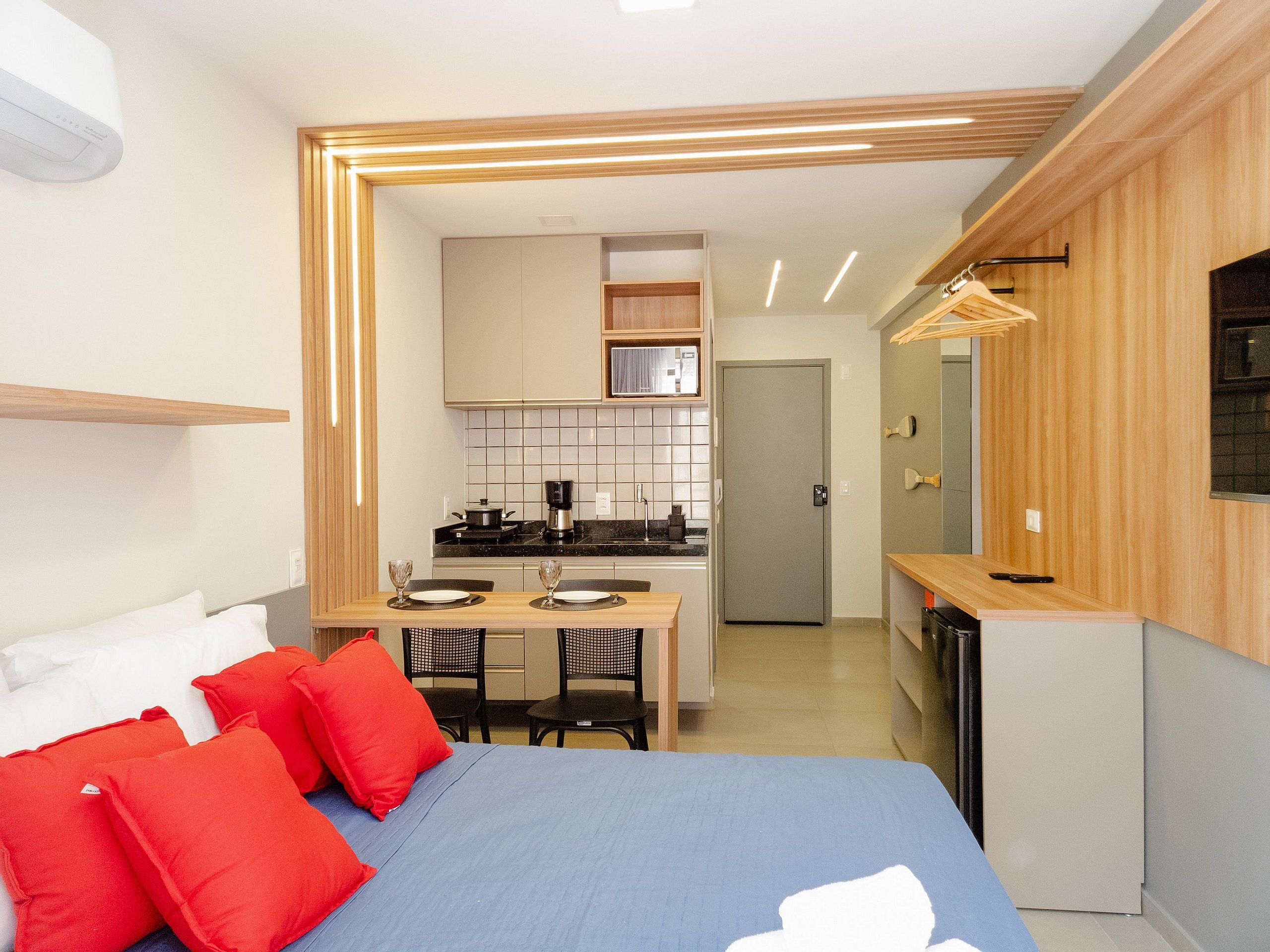 Quarto de hotel moderno com cama, escrivaninha e cozinha compacta.