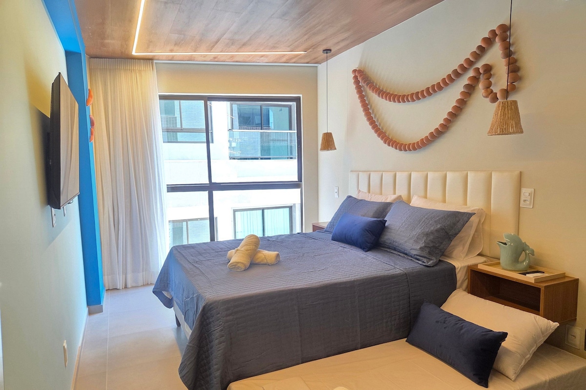 Quarto de hotel com uma cama grande, mesa de cabeceira, televisão na parede e uma janela com cortinas.