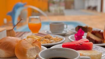 Uma mesa posta para o café da manhã, com uma xícara de café, um copo de suco de laranja e diversos alimentos.