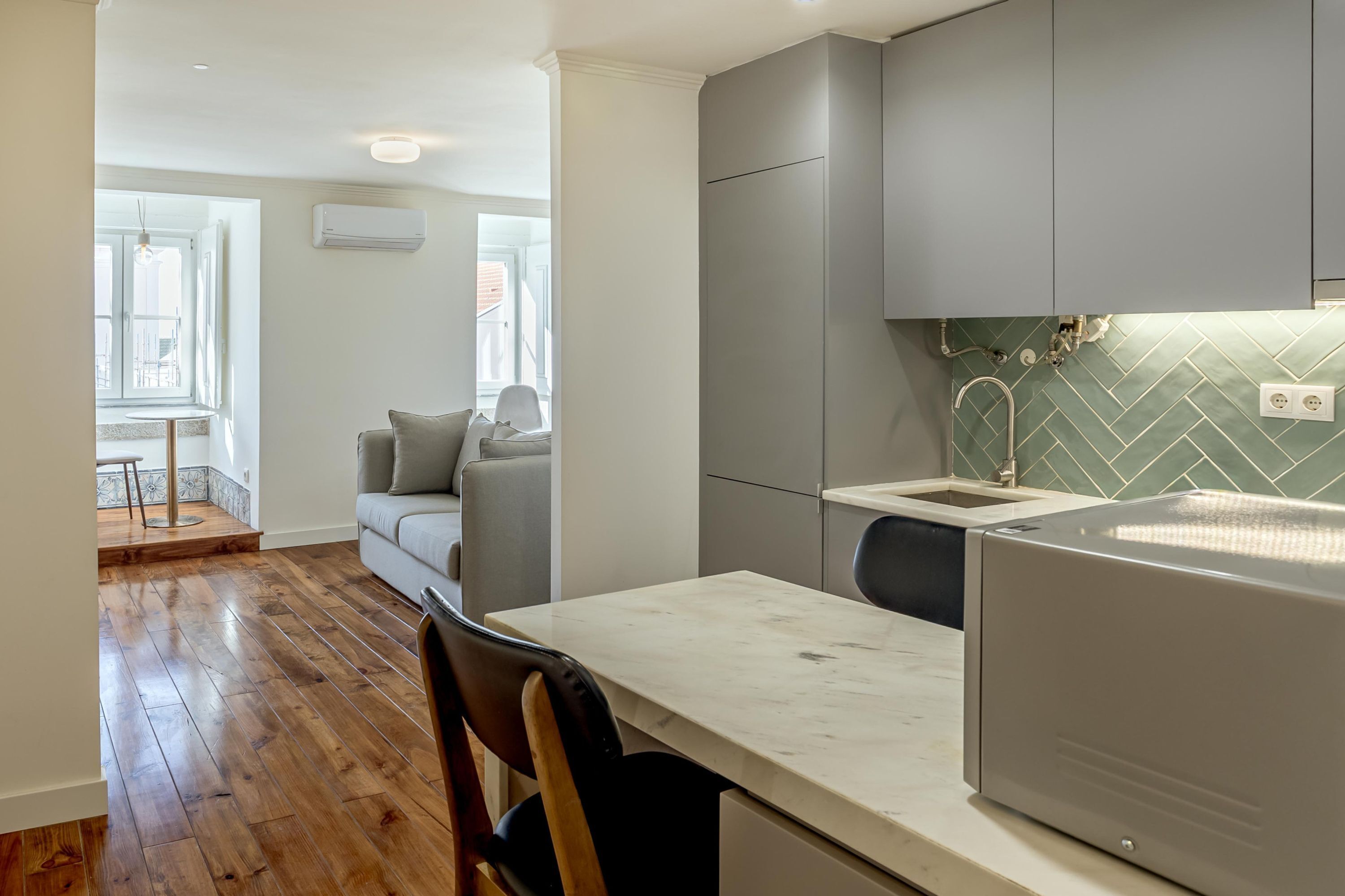 Uma cozinha moderna com armários cinza, bancada de mármore e backsplash em padrão herringbone.