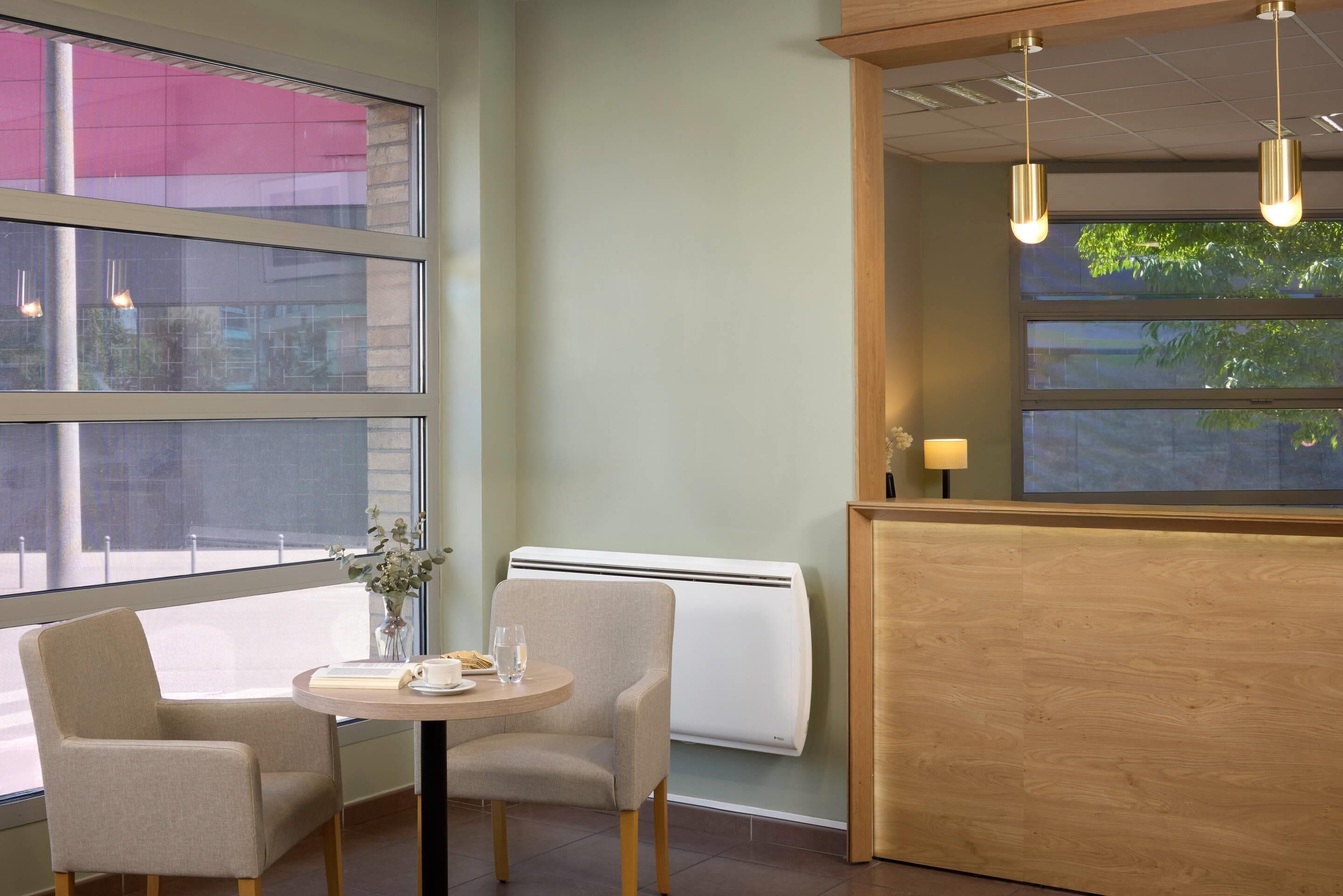 Quarto de hotel moderno com uma mesa redonda, duas cadeiras, um vaso com flores e uma mesa de recepção.