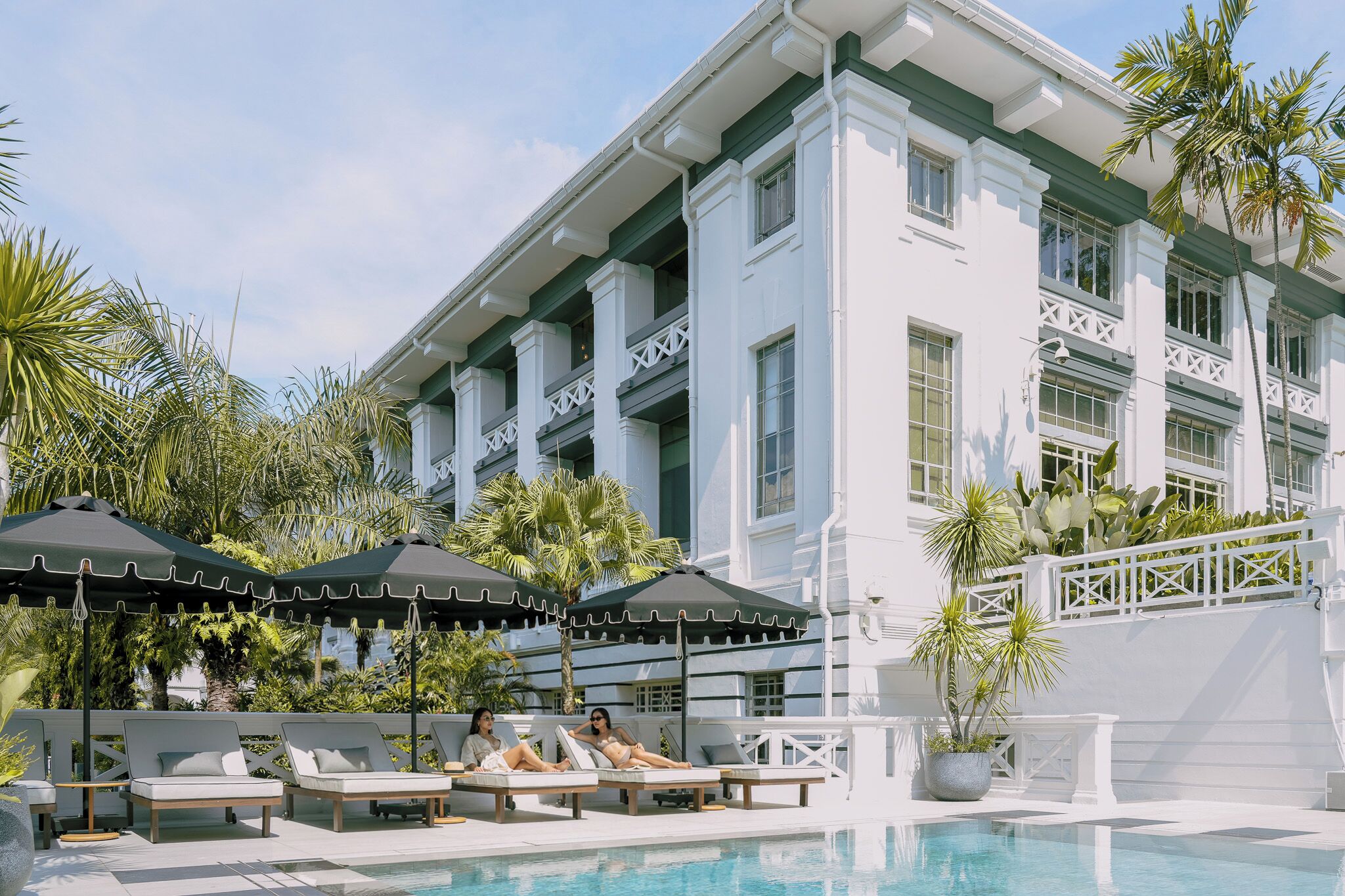 Um hotel com área de piscina, mobiliário de exterior e palmeiras.