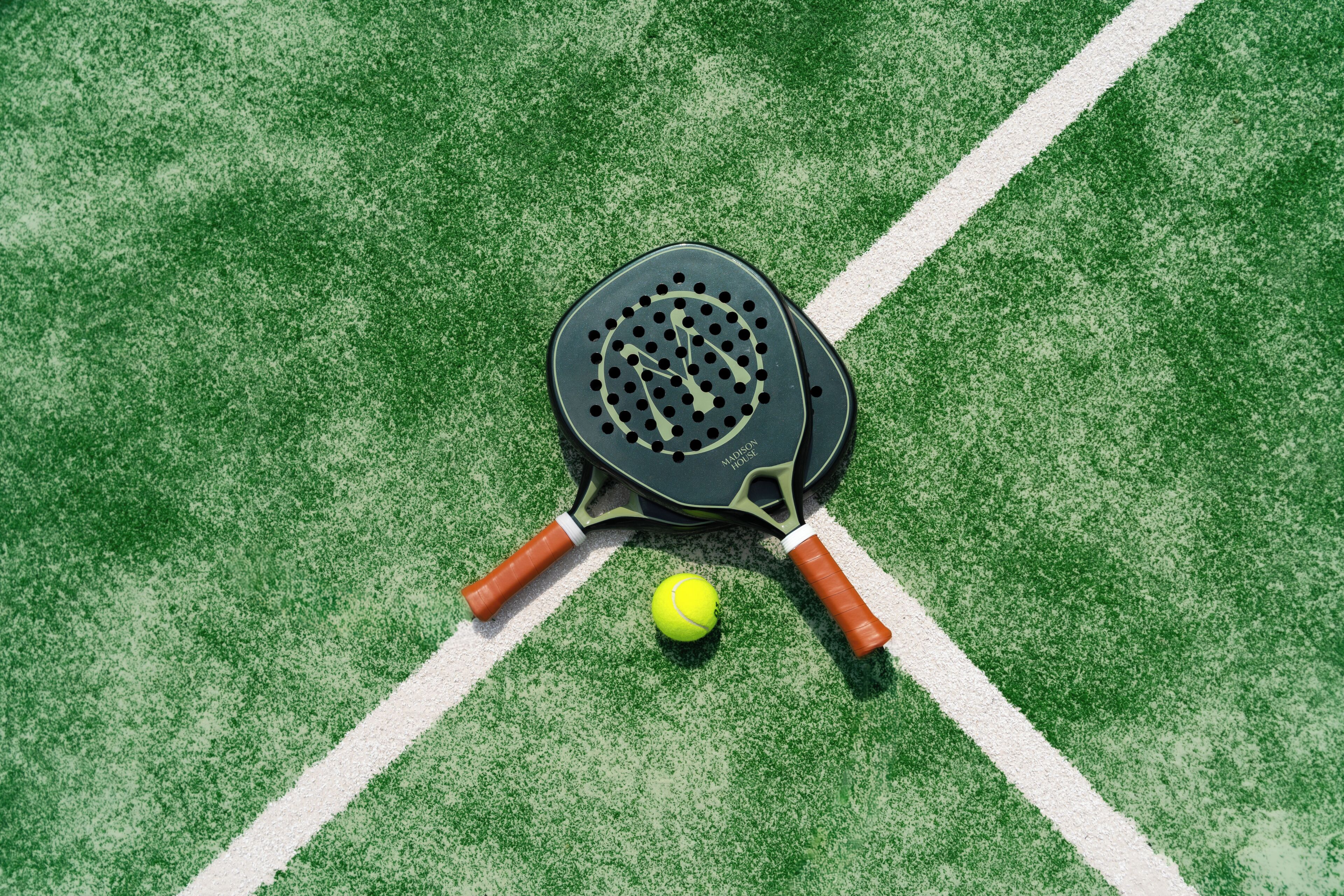 Uma raquete de tênis e uma bola em quadra verde com linhas brancas.