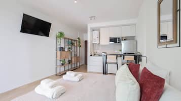 Quarto de hotel moderno com cama, televisão de tela plana, cozinha compacta e pequena área de refeições.