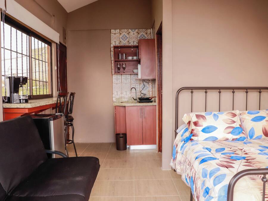 Quarto compacto com cama, pequena cozinha, área de refeições e janela.