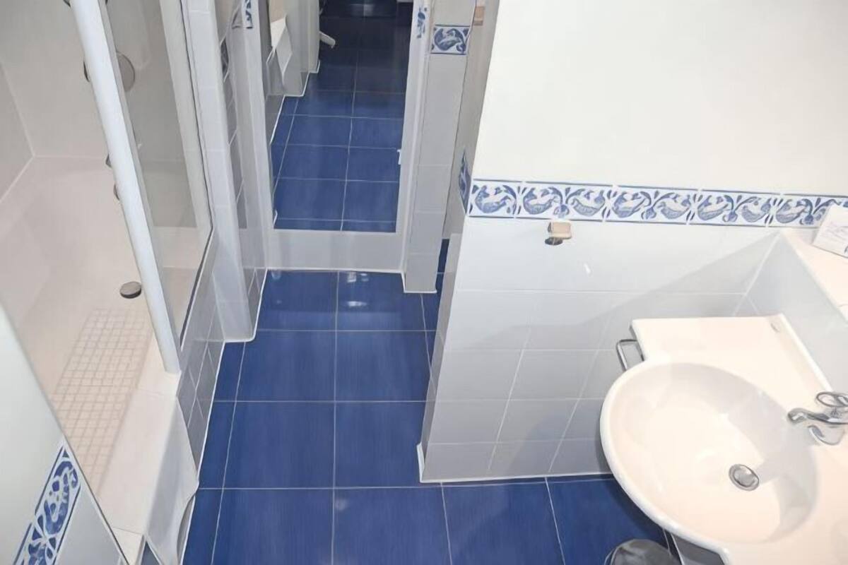 Um banheiro com piso de azulejos azuis, pia branca e parede revestida com uma moldura decorativa.