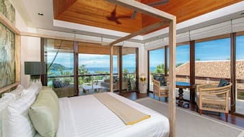 Um quarto espaçoso com uma cama grande, uma varanda com móveis de vime e vista para o oceano.