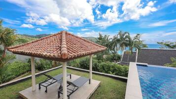 Uma área de piscina no terraço com um pergolado revestido, espreguiçadeiras e vista para o oceano.