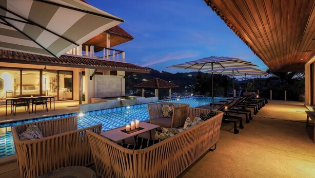 Uma área de piscina no terraço com assentos e guarda-sóis, com vista para um horizonte urbano ao entardecer.
