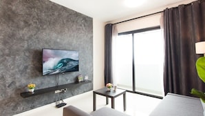 Uma sala de estar moderna com televisão de tela plana presa a uma parede texturizada, um sofá, uma mesinha de centro com uma planta e uma janela grande com cortinas.
