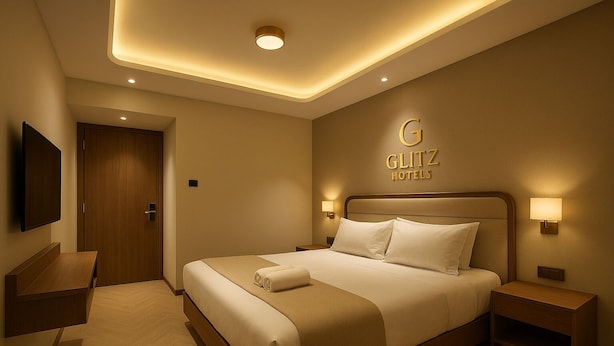 Quarto de hotel com uma cama grande, televisão na parede, mesa de cabeceira de madeira e luminária no teto.