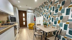Cozinha moderna com área de refeições, destacando uma mesa e cadeiras de madeira, uma poltrona amarela e um papel de parede estampado.