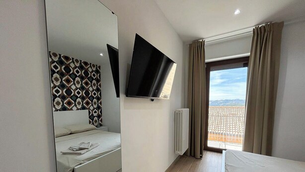 Quarto de hotel com cama, um espelho grande, televisão de tela plana, radiador e janela com cortinas.