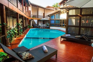 Uma área de piscina com deck de madeira, espreguiçadeiras e um espaço coberto para sentar.