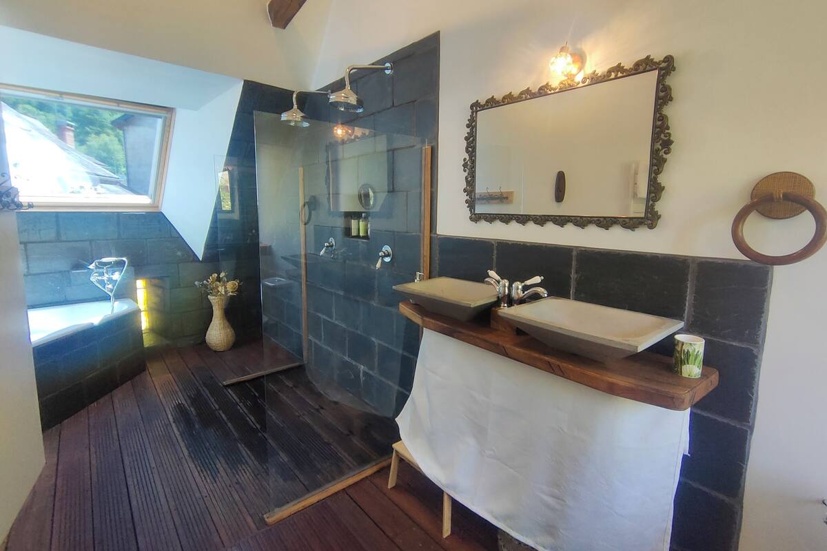 Casa de banho com chuveiro envidraçado, duas pias, um espelho e uma janela.