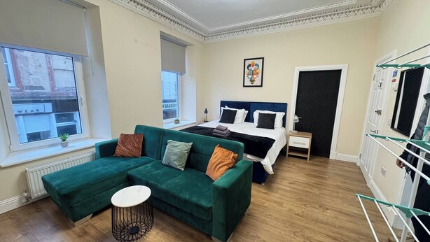 Quarto moderno com um sofá seccional verde, uma cama grande com cabeceira azul e uma pequena mesa de cabeceira.