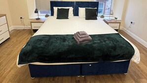 Quarto bem arrumado com uma cama grande, duas mesas de cabeceira, um espelho e vista da rua pelas janelas.