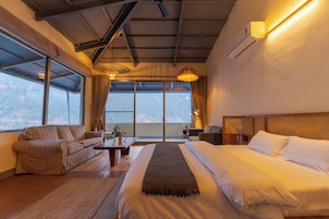 Quarto de hotel moderno com uma cama grande, um sofá, uma mesa pequena e vista para o exterior.