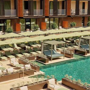 Área de piscina no terraço com várias espreguiçadeiras e guarda-sóis, cercada por um edifício moderno com varandas.
