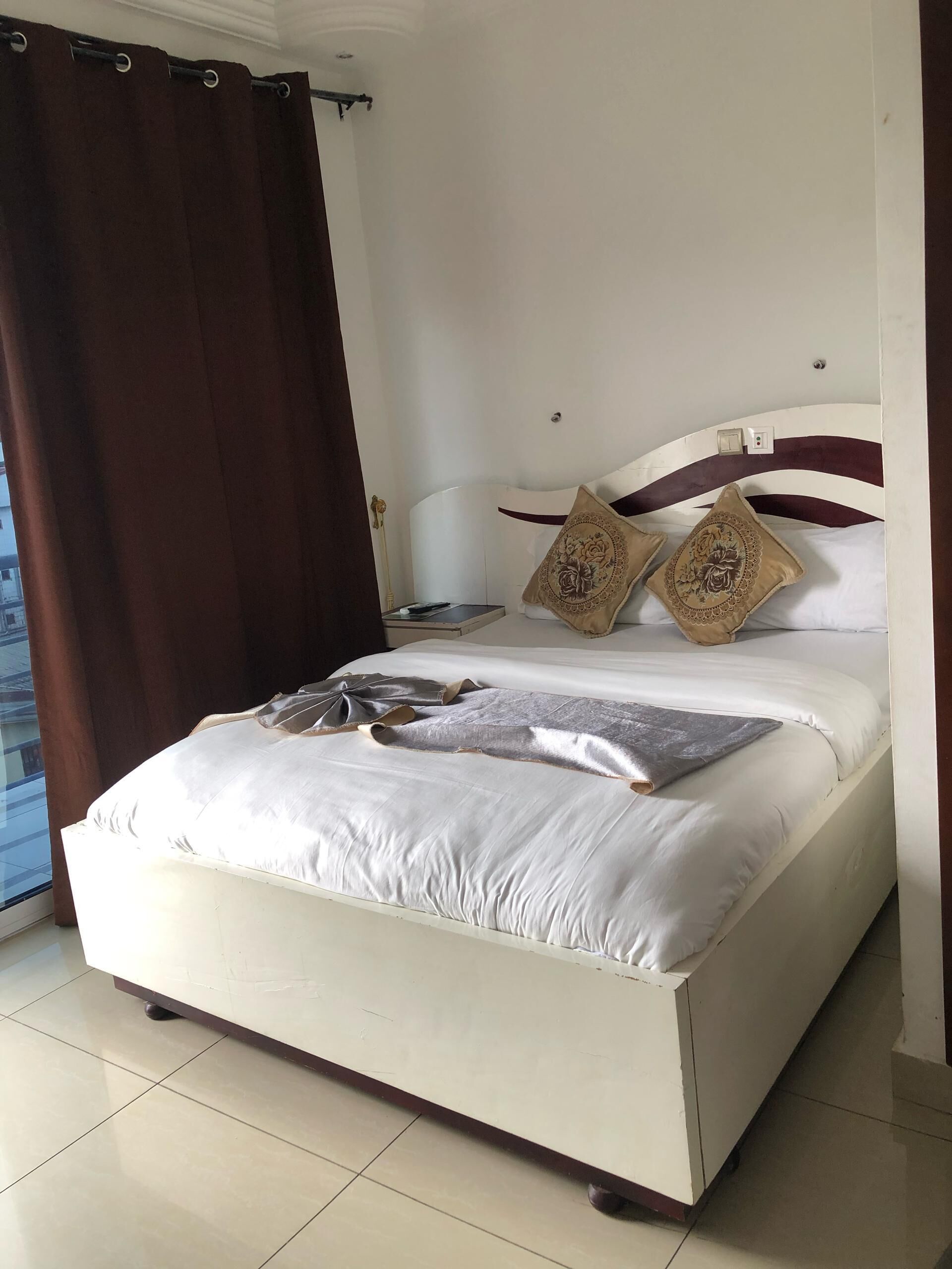 Cama bem arrumada com lençóis brancos, duas almofadas decorativas e uma bandeja de metal.