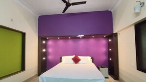 Quarto com cama, ventoinha no teto, mesa de cabeceira e luminária fixada na parede.