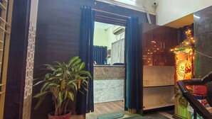 Um quarto com porta de madeira escura, um vaso de planta, piso de mármore e um pequeno santuário com luzes.