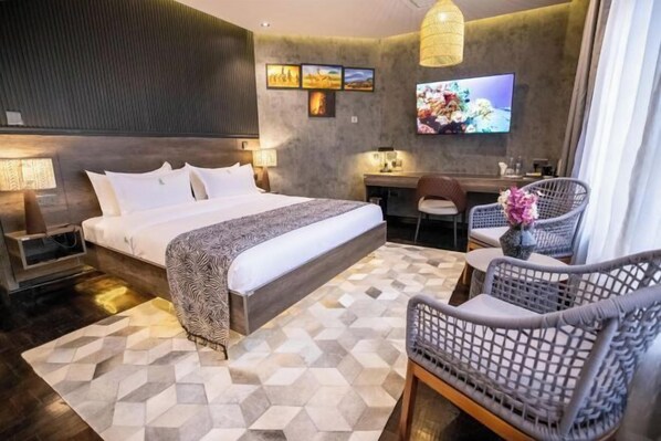 Quarto de hotel moderno com uma cama grande, uma escrivaninha, uma cadeira e uma TV na parede.