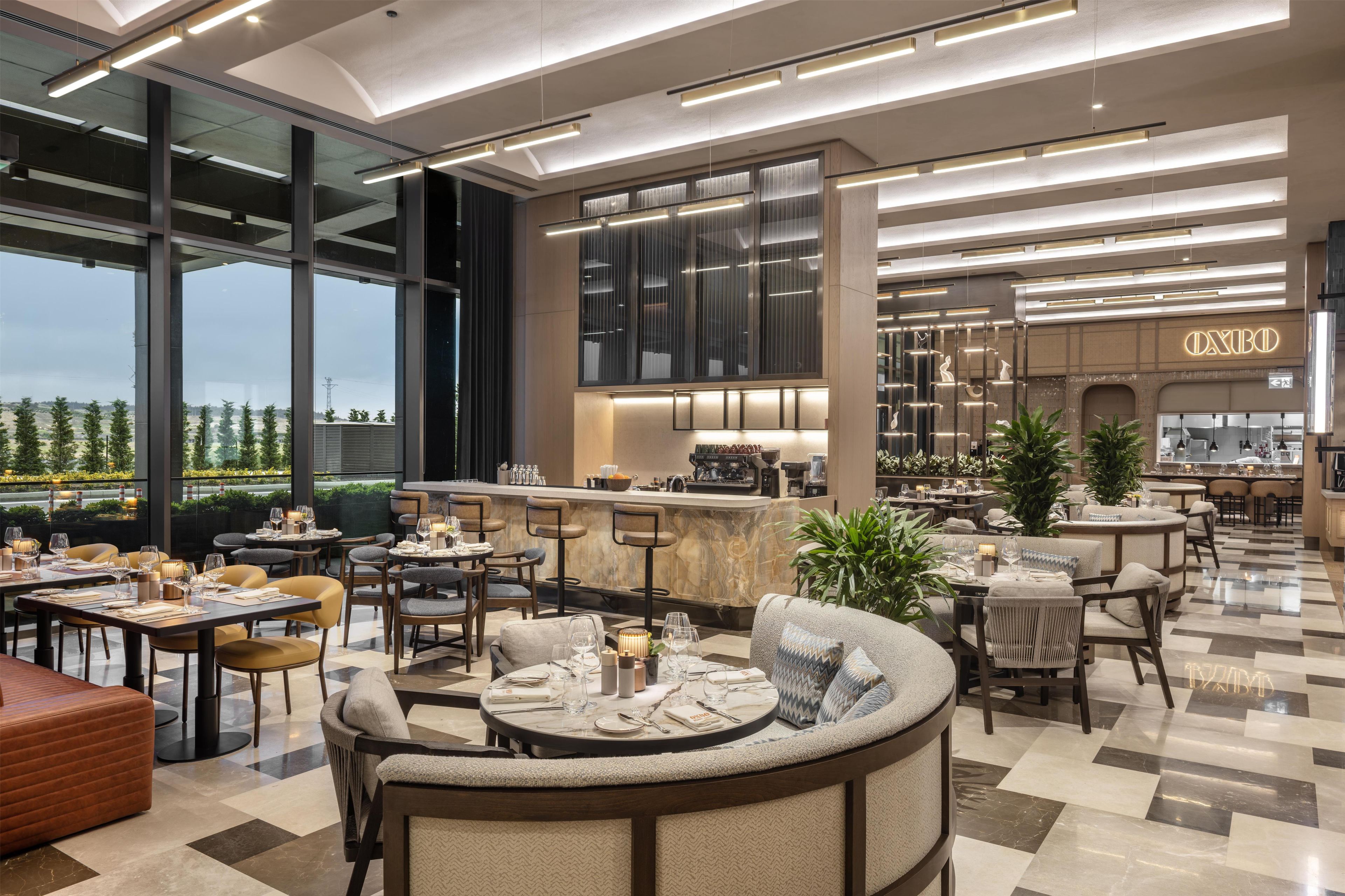 Um lobby de hotel moderno com área de bar, assentos e vista para o exterior.