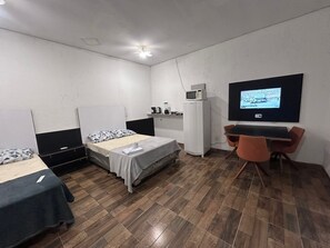 Quarto compacto com duas camas, uma escrivaninha, televisão e micro-ondas.