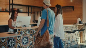 Bancada com azulejos estampados, máquina de café e algumas cadeiras ao fundo.