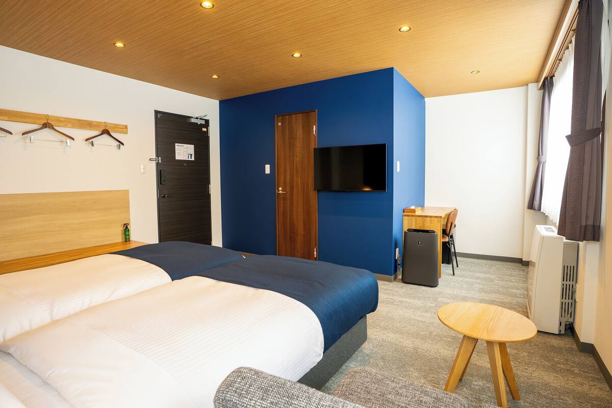 Quarto de hotel com duas camas, uma escrivaninha, uma televisão e uma mesinha.