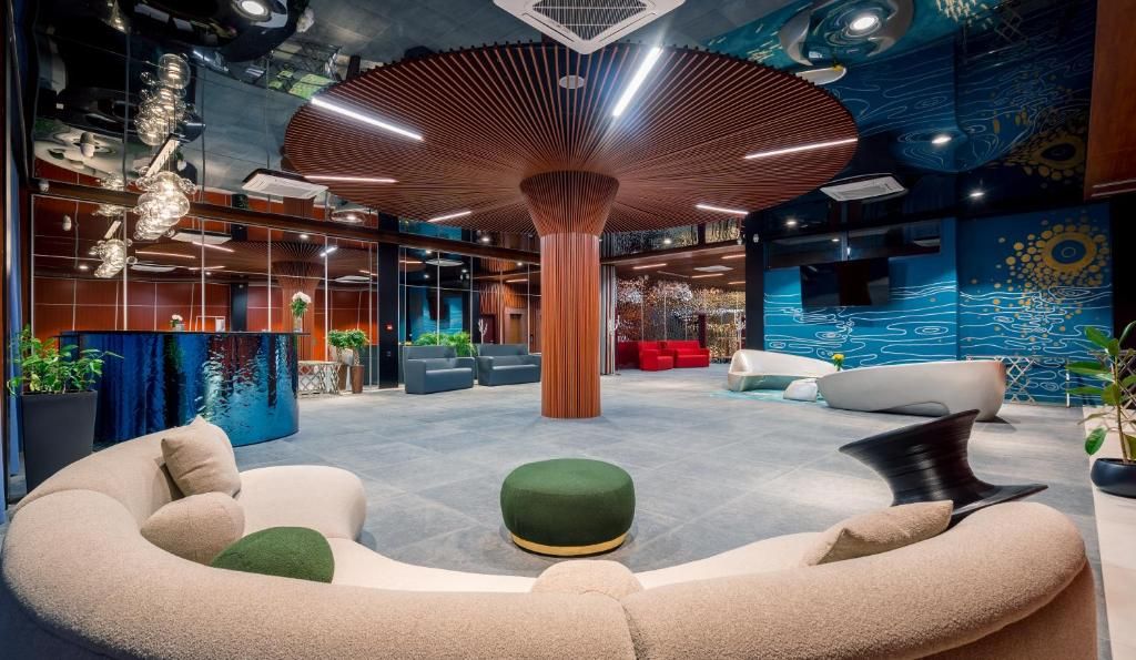 Um lobby moderno com uma coluna central de madeira, áreas de estar e um mural vibrante.
