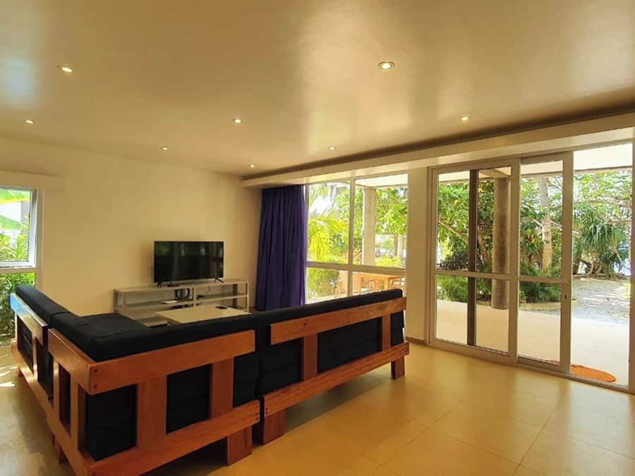 Quarto espaçoso com um banco de madeira grande, uma televisão e uma porta de vidro deslizante que dá para um jardim.