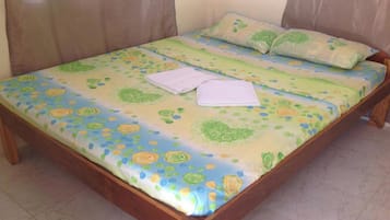 Uma cama com roupa de cama florida e duas almofadas, cabeceira de madeira e parede lisa.