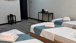 Quarto de hotel com três camas, uma mesinha com telefone, televisão na parede e uma porta.