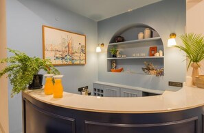 Bancada de recepção com parede azul, um quadro emoldurado e uma estante com objetos decorativos.