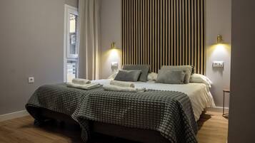 Uma cama bem arrumada com colcha estampada, duas luminárias de cabeceira e um painel de madeira vertical na parede.