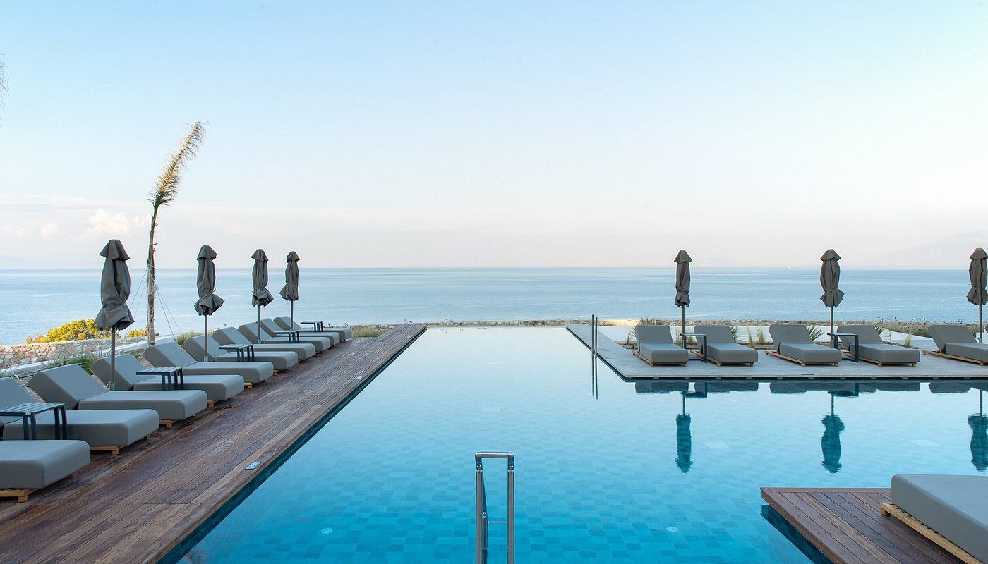Área de piscina com espreguiçadeiras e guarda-sóis, com vista para um mar tranquilo.