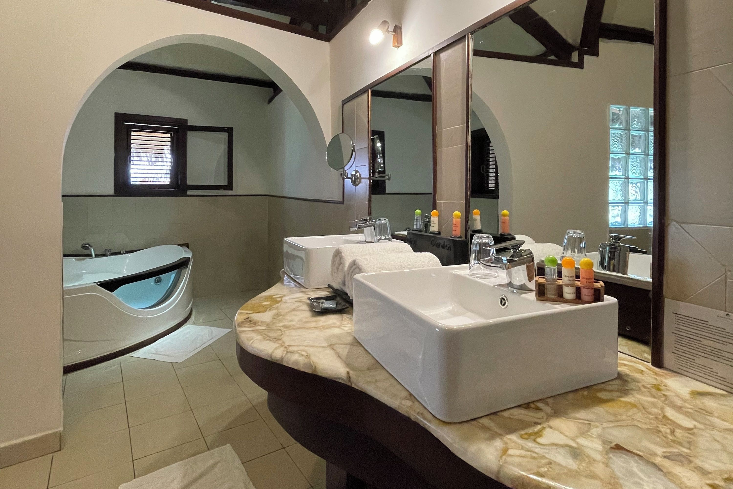 Uma casa de banho moderna com um espelho grande, duas bacias, uma banheira e um lavatório com artigos de higiene pessoal.