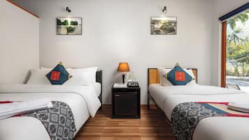 Quarto de hotel com duas camas, uma mesa de cabeceira, uma luminária e duas fotografias emolduradas na parede.