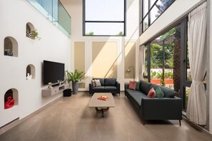 Sala de estar moderna com televisão de tela plana, dois sofás, uma mesa de centro e uma janela grande com vista para o verde.