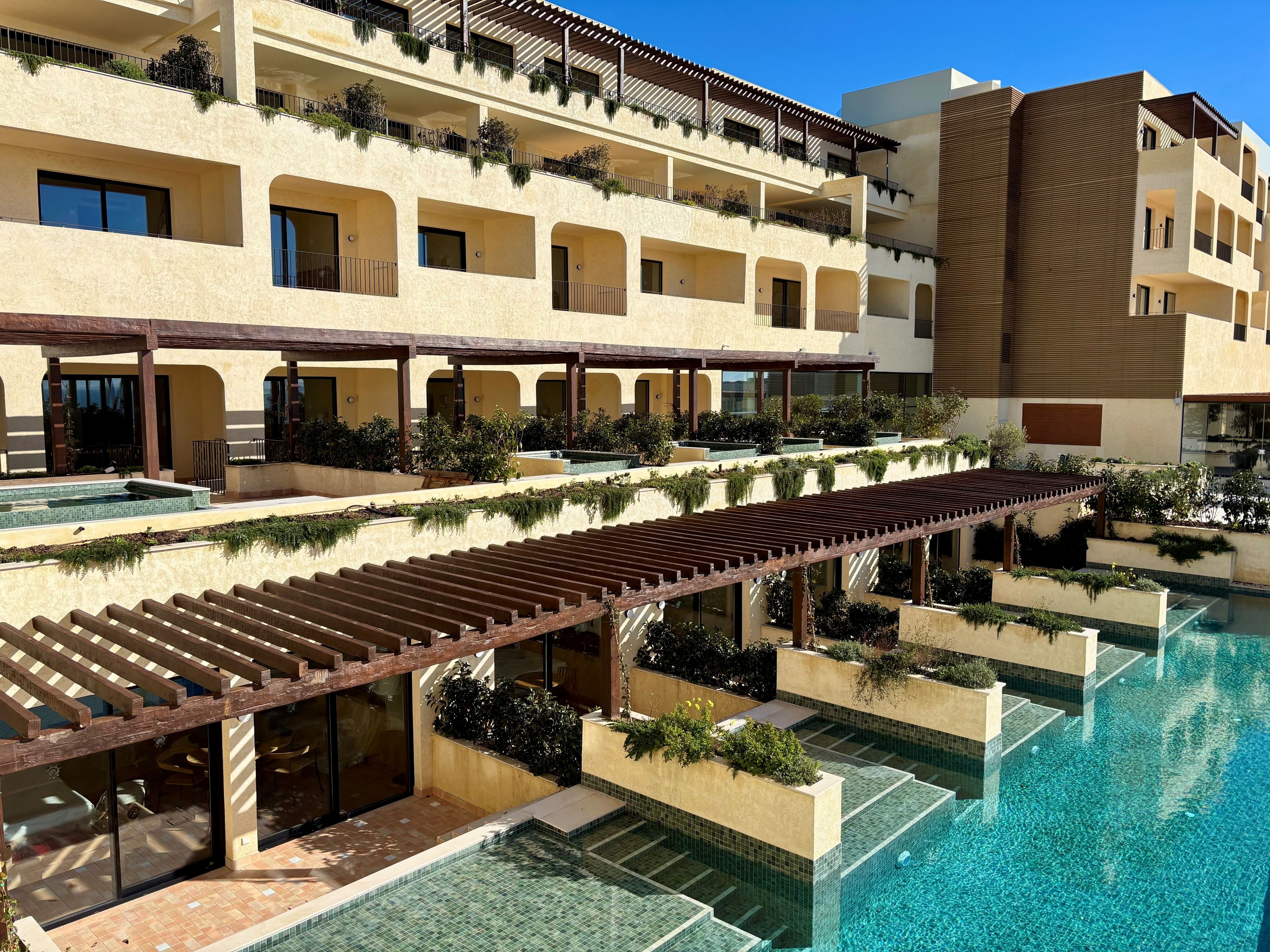 Um hotel com piscina, área de estar externa e varandas com plantas.