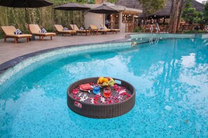 Área da piscina com espreguiçadeiras e uma cesta flutuante com frutas e bebida.