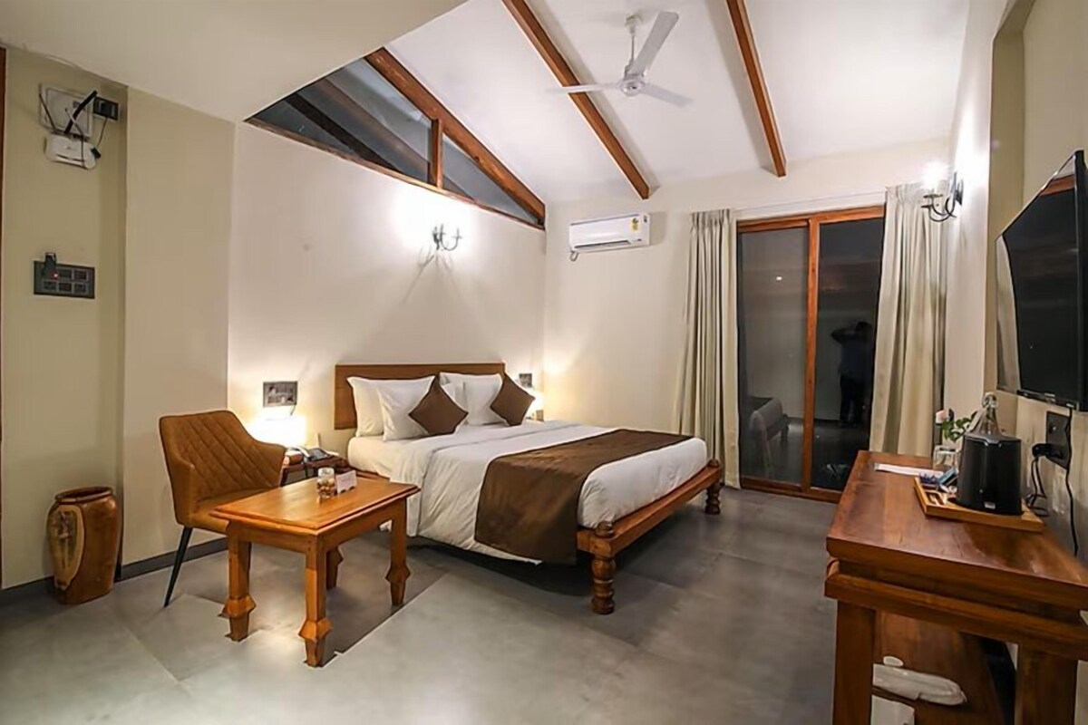 Quarto de hotel com cama, escrivaninha, cadeira, ventilador de teto e porta de vidro deslizante.