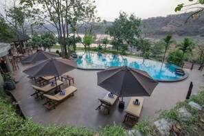 Área de piscina com espreguiçadeiras e guarda-sóis, cercada por árvores e vista para colinas.