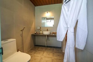 Casa de banho com sanita, lavatório e chuveiro. Um roupeiro branco está pendurado na parede.