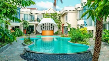 Área de piscina com um edifício moderno ao fundo, cercada por vegetação exuberante.