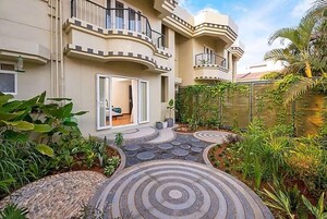 Edifício residencial com vários andares, varandas, um caminho de jardim pavimentado e vegetação ao redor.